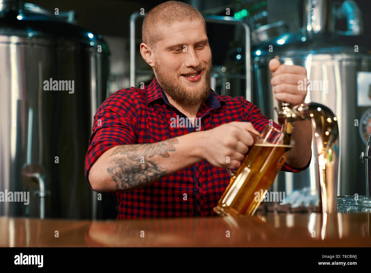 Front view of male barmen working in pub and pouring ale in glass ...