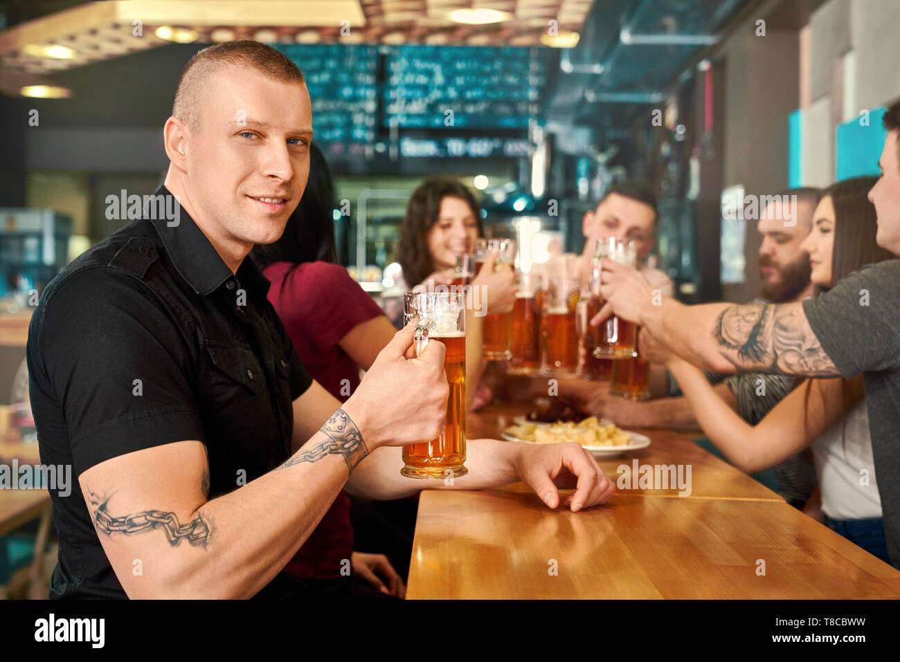 Side view of tattooed man in black shirt keeping glass of beer, looking ...