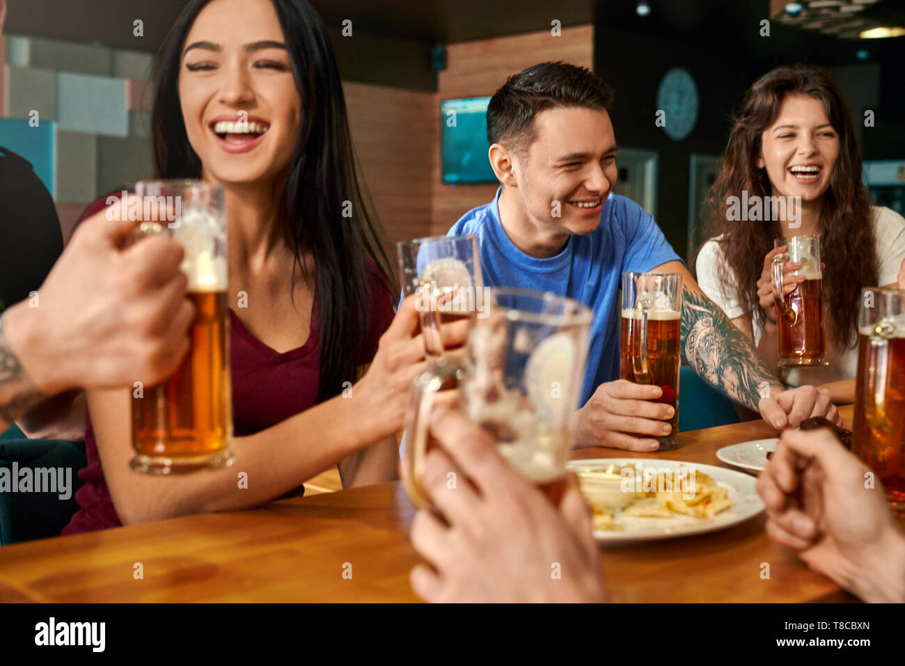 Happy company laughing and joking while drinking tasty beer in pub ...