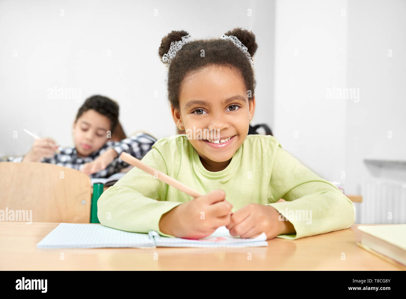 Pretty, beautiful girl, schoolchild smiling, sitting at desk, holding ...