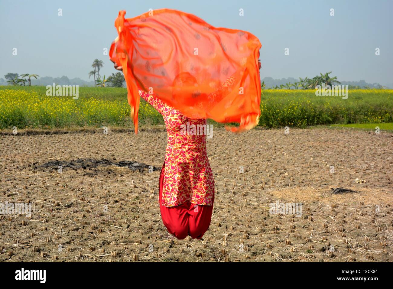 A girl wearing a salwar kameez flying a red dhupatta / clothin the air ...