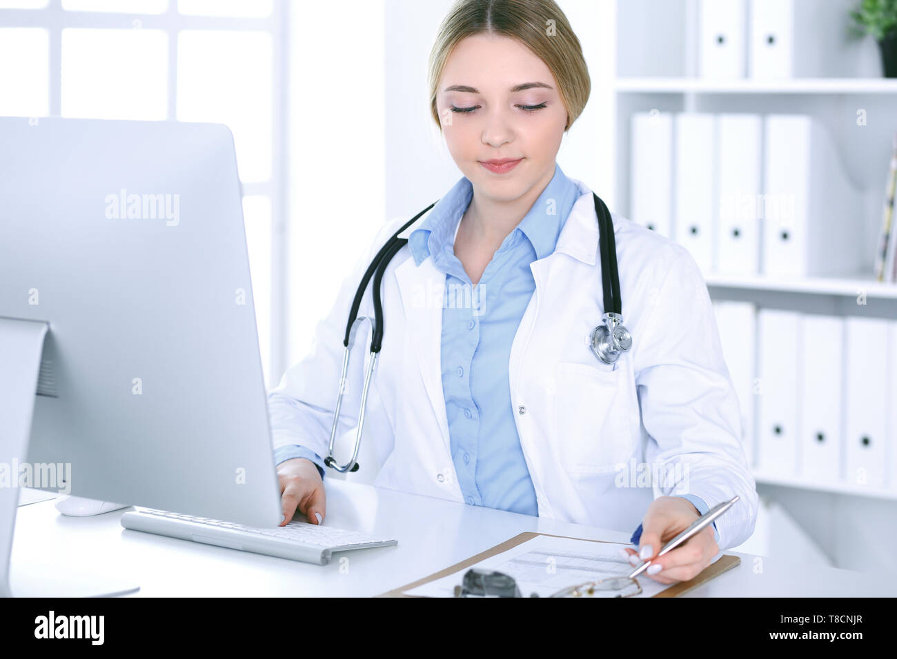 Young woman doctor at work in hospital looking at desktop pc monitor ...