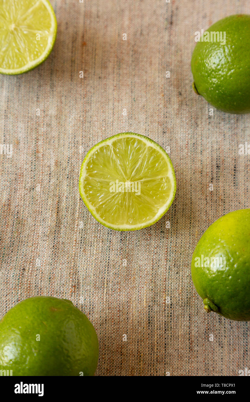 Whole and cut green citrus limes on cloth, overhead view. From above ...