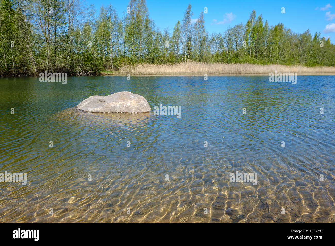 clear transparent water lake with sand bottom and large rock in the ...