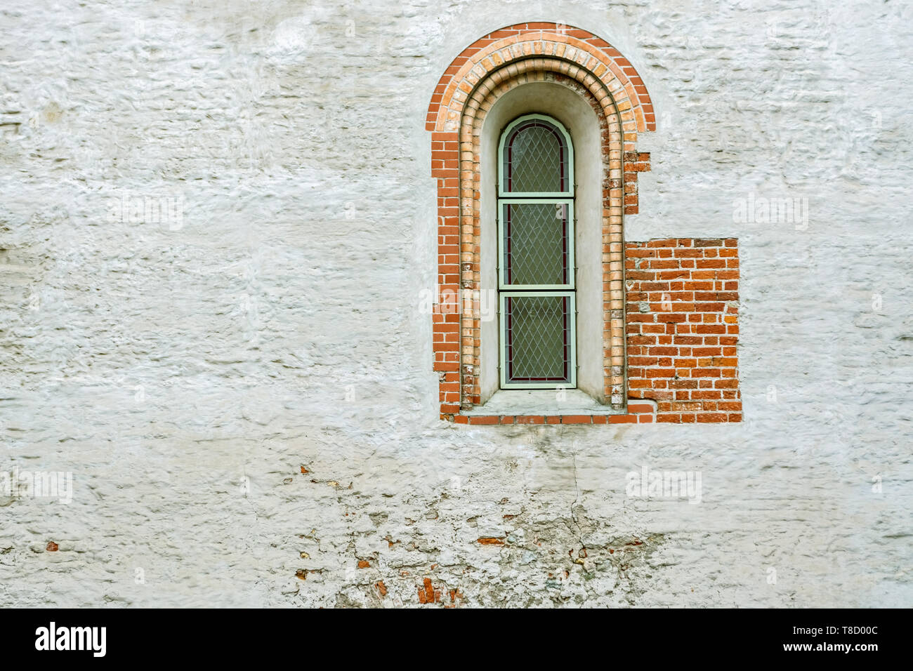 Narrow arched window with bars on the brick plastered wall in old Riga ...