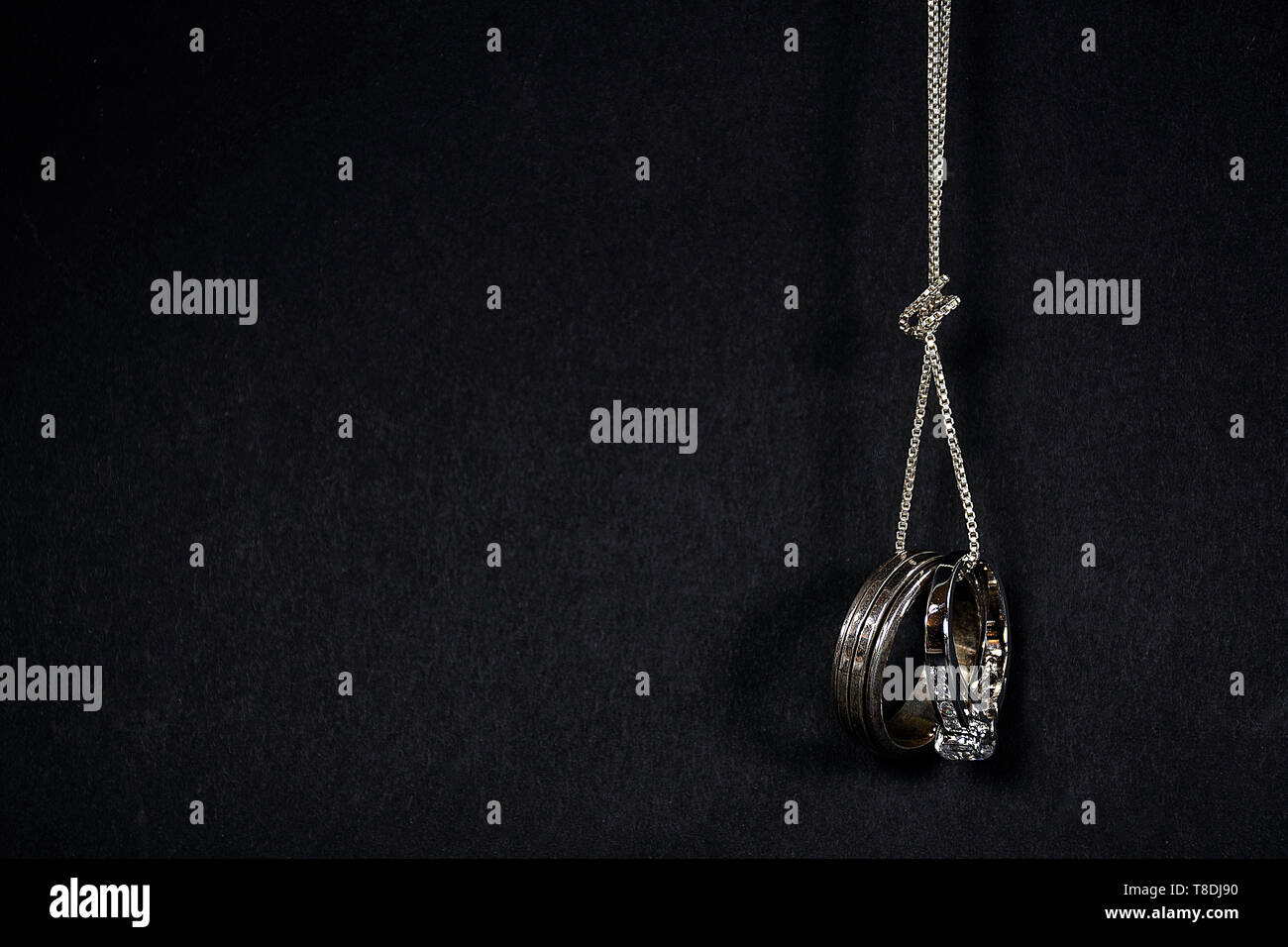 pair of wedding rings hanging from a silver chain with knot isolated on ...