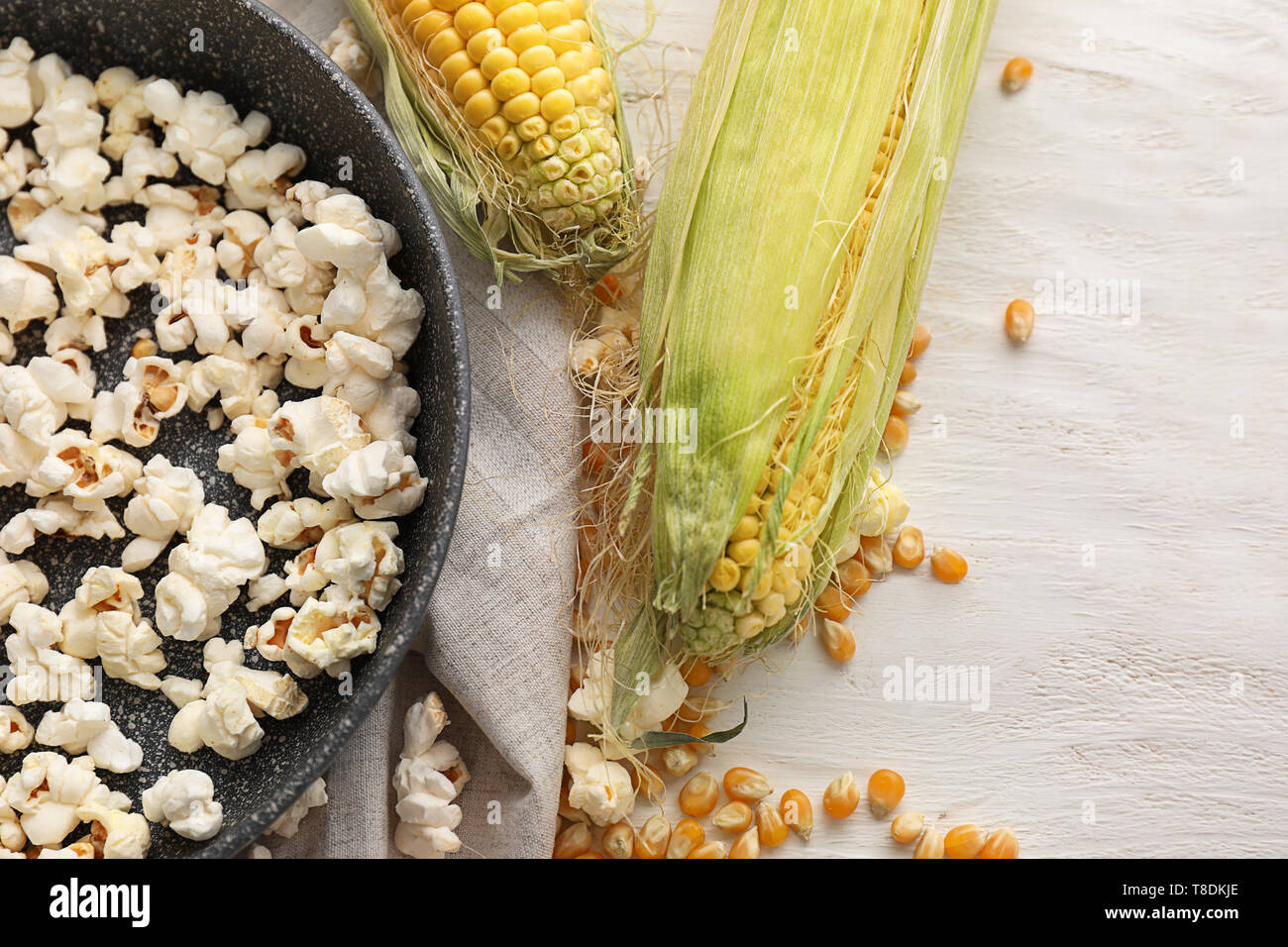 Frying pan with delicious popcorn and cobs on wooden background Stock ...