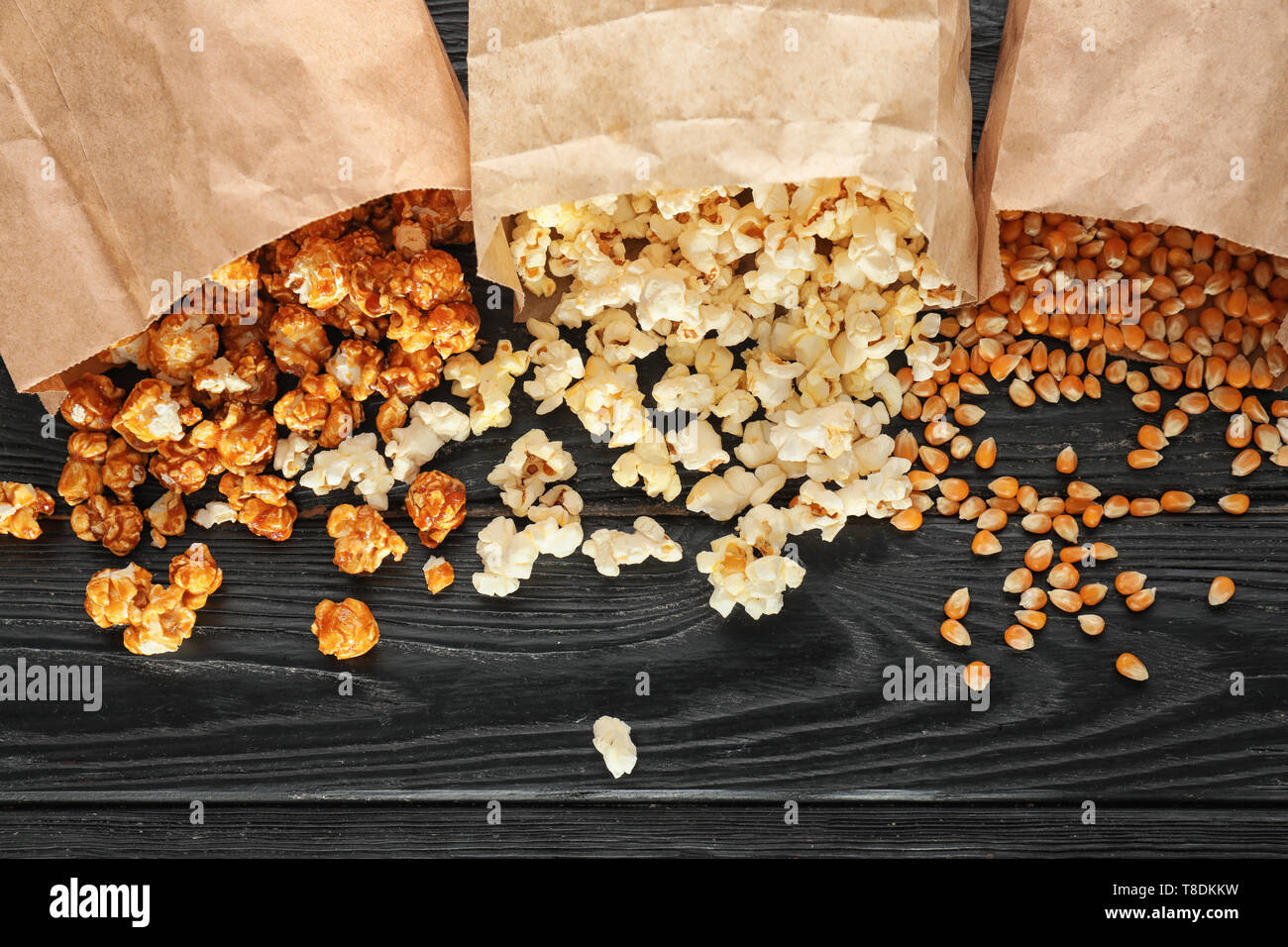 Paper bags with scattered delicious popcorn and kernels on wooden ...