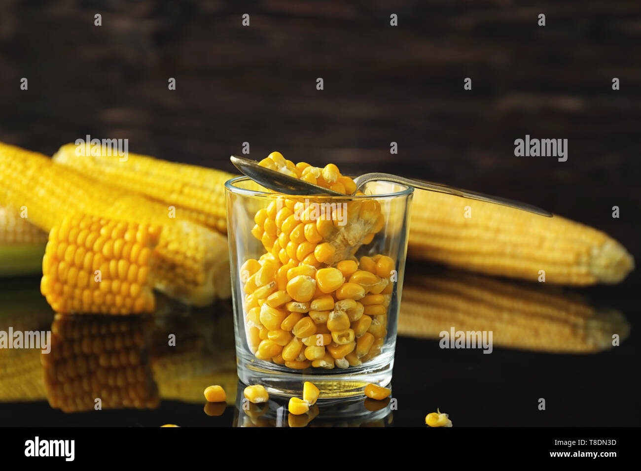 Glass with tasty corn kernels on table against dark background Stock ...
