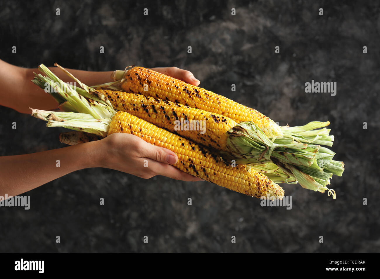 Woman holding grilled corn cobs on grey background Stock Photo - Alamy