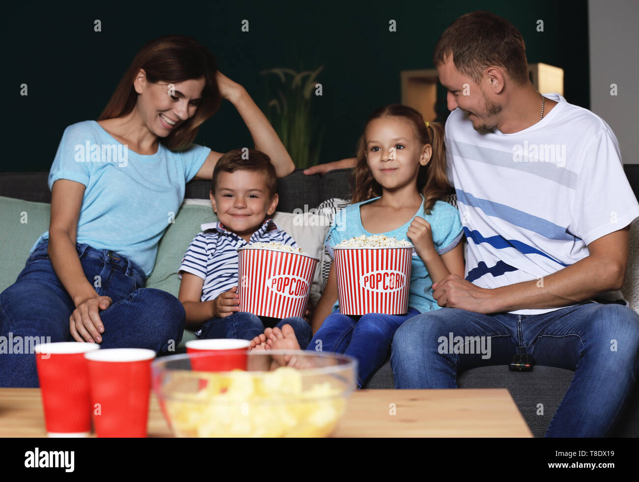 Happy family eating popcorn while watching TV in evening Stock Photo ...
