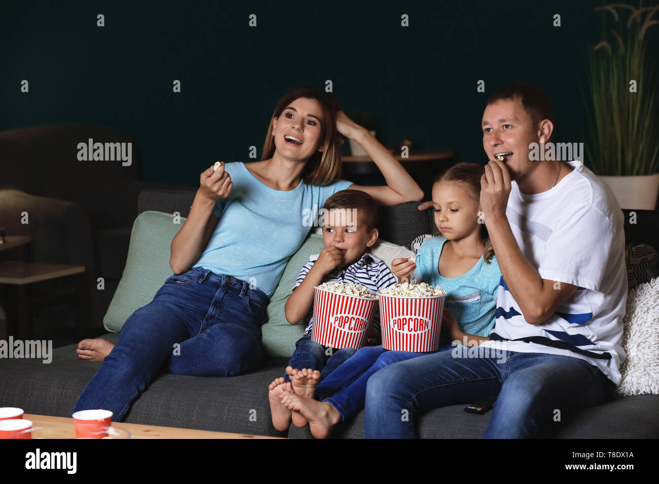 Happy family eating popcorn while watching TV in evening Stock Photo ...