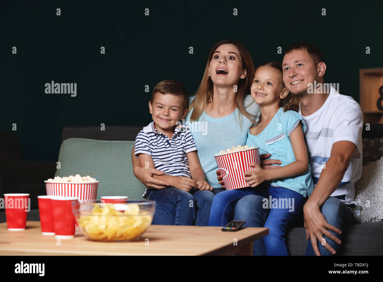 Happy family eating popcorn while watching TV in evening Stock Photo ...