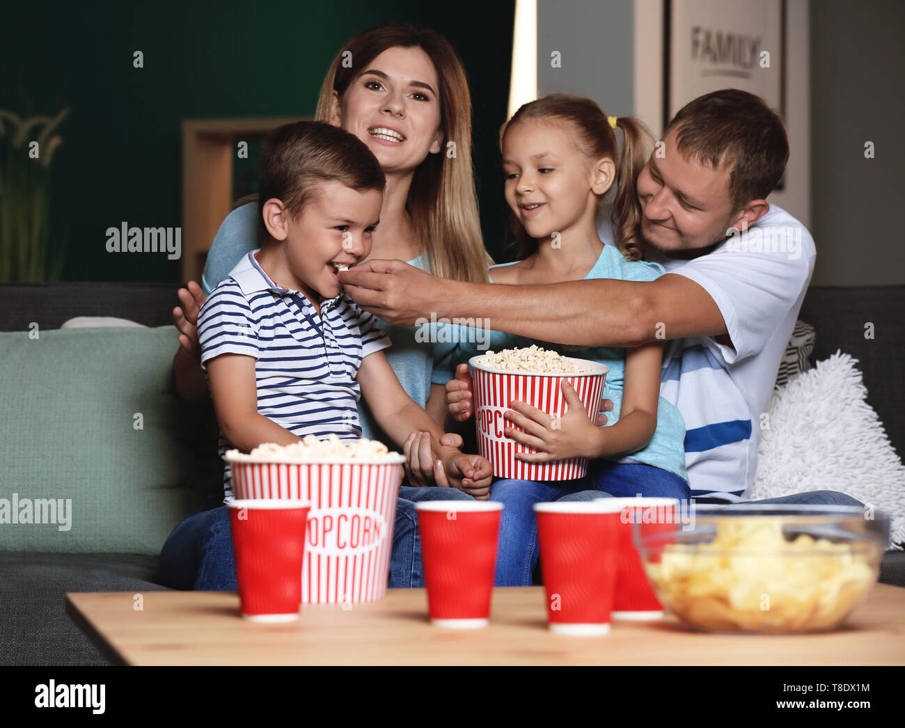 Happy family eating popcorn while watching TV in evening Stock Photo ...