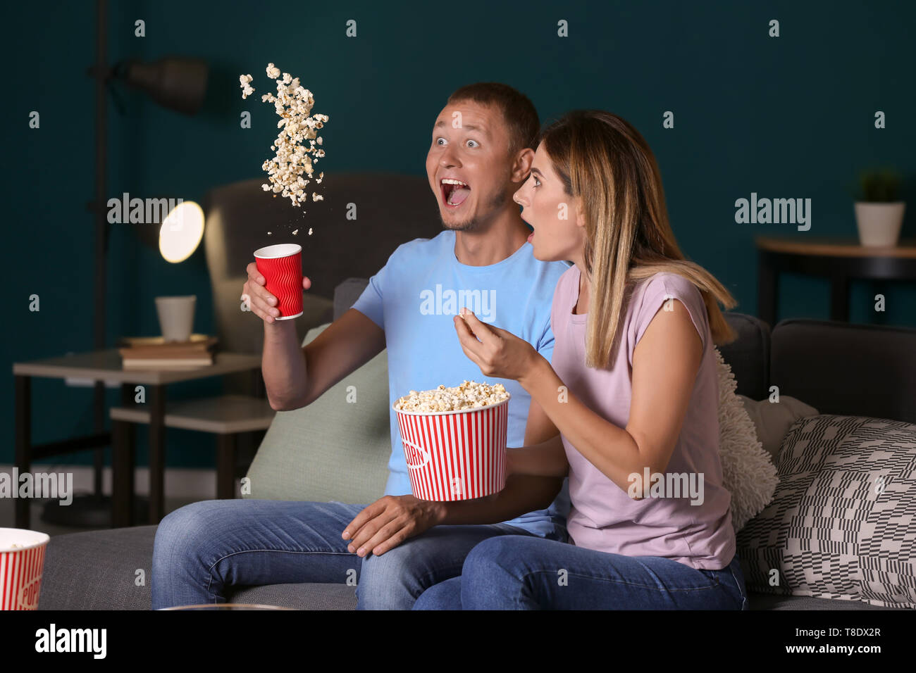 Happy emotional couple eating popcorn while watching TV in evening ...