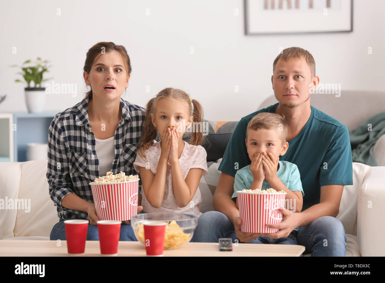 Family eating popcorn while watching scary movie at home Stock Photo ...