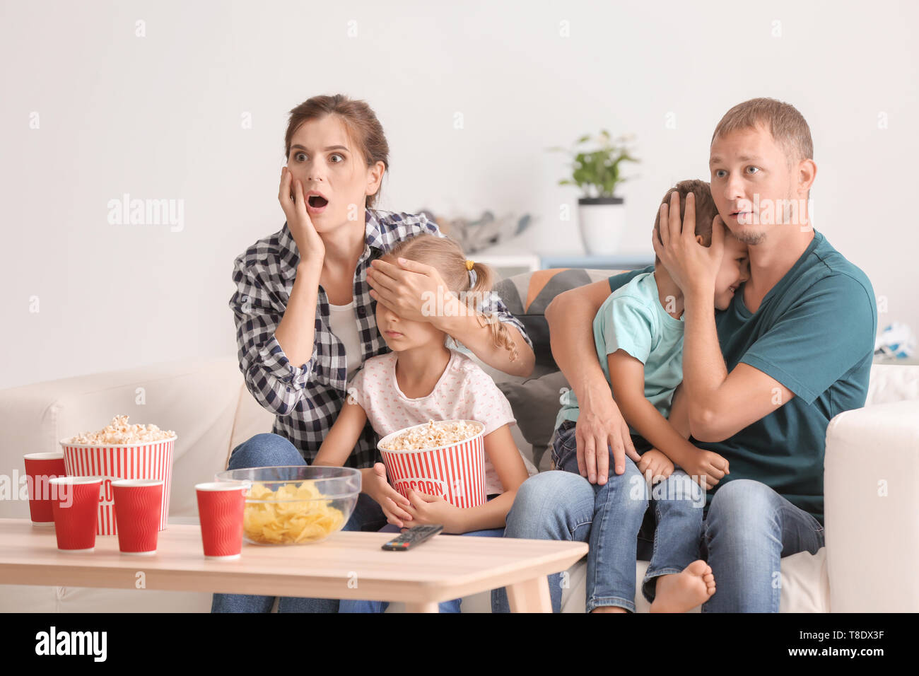 Family eating popcorn while watching scary movie at home Stock Photo ...