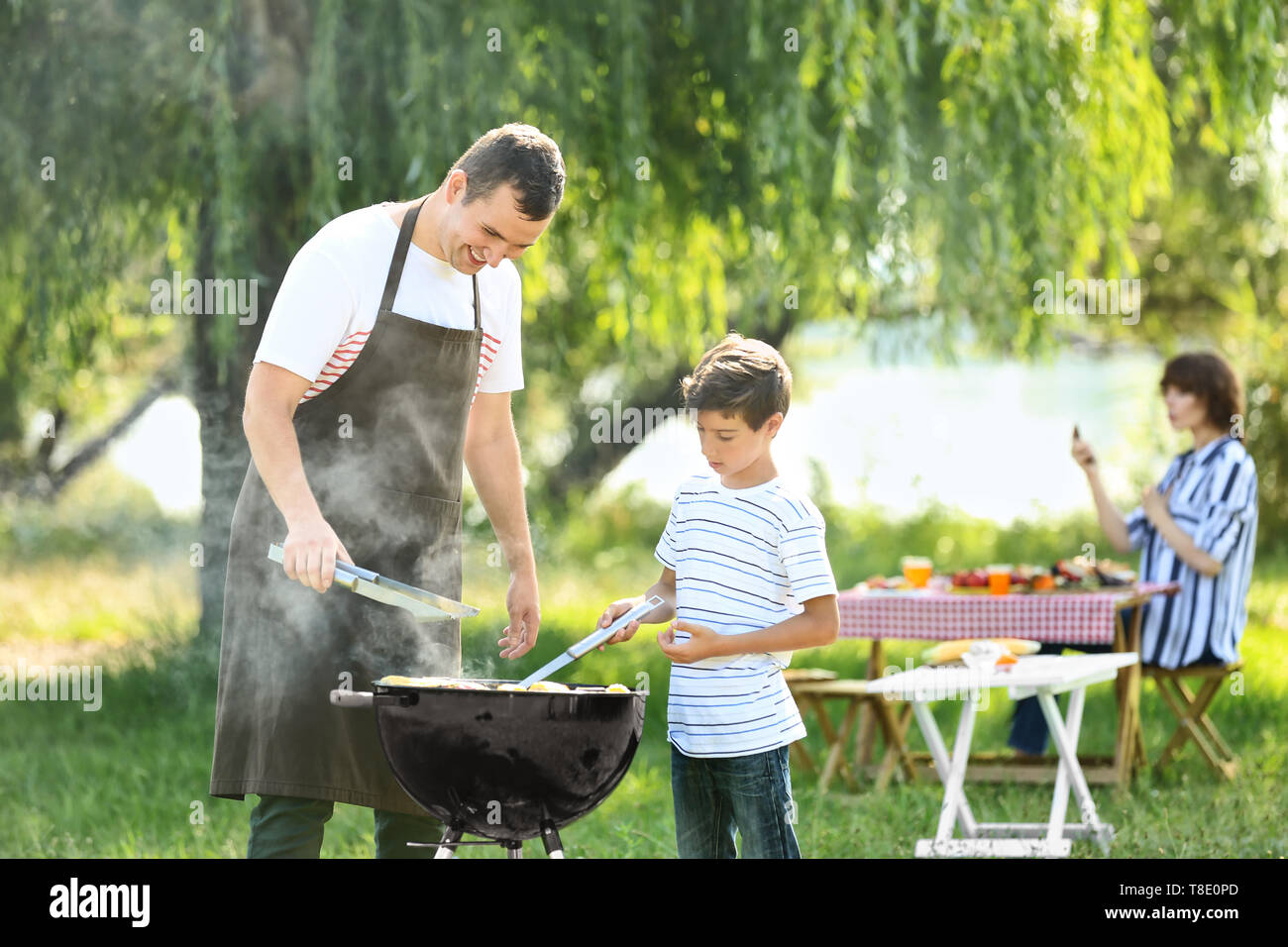 Little boy with his father cooking tasty food on barbecue grill ...