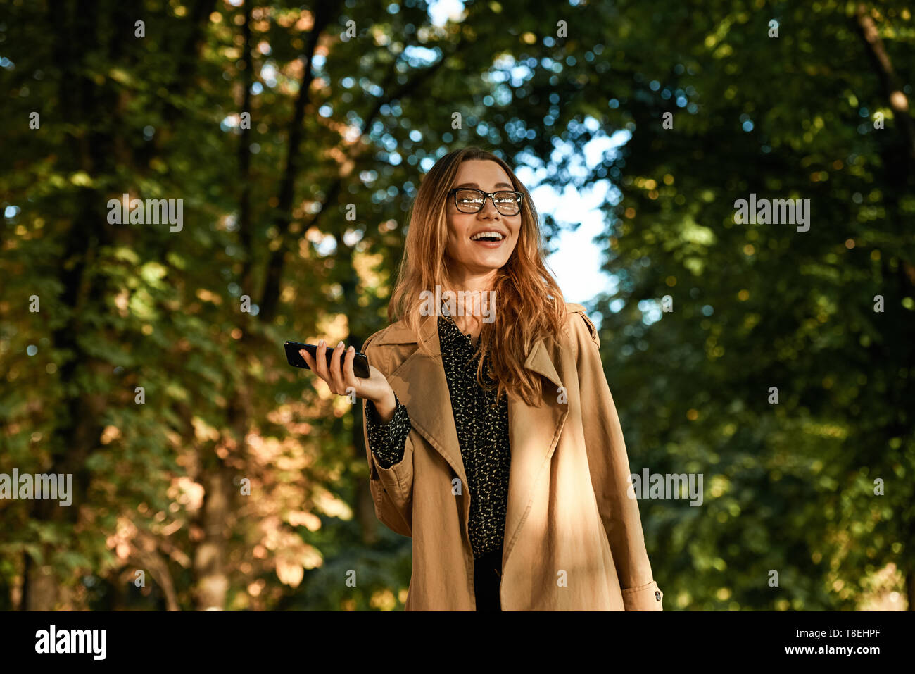 Portrait of lovely woman 20s wearing coat and eyeglasses using cell ...