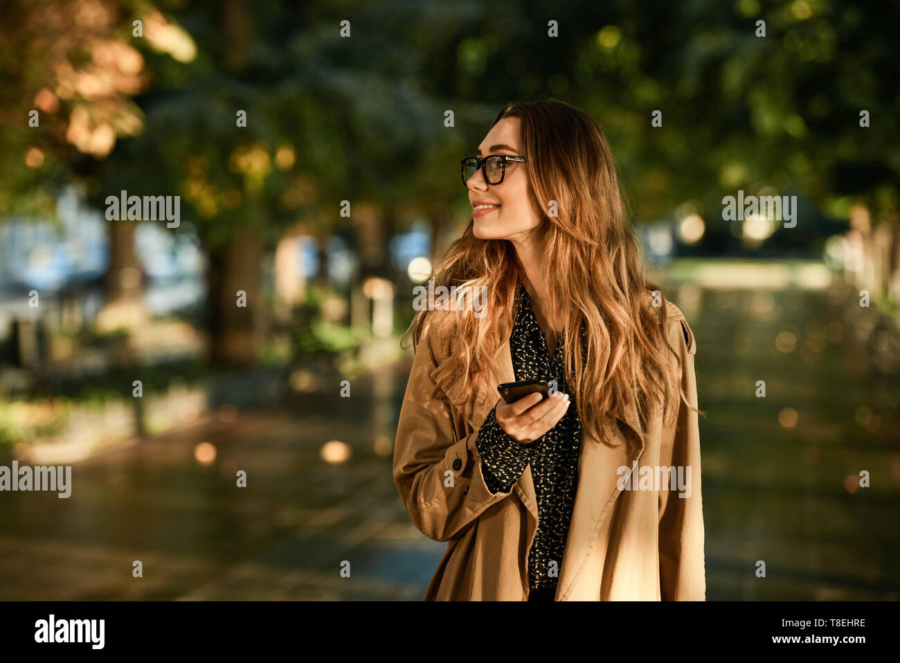 Portrait of brunette woman 20s wearing coat and eyeglasses using cell ...
