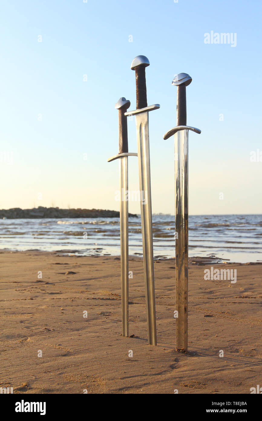 Three swords in sand of battlefield on sea beach Stock Photo - Alamy