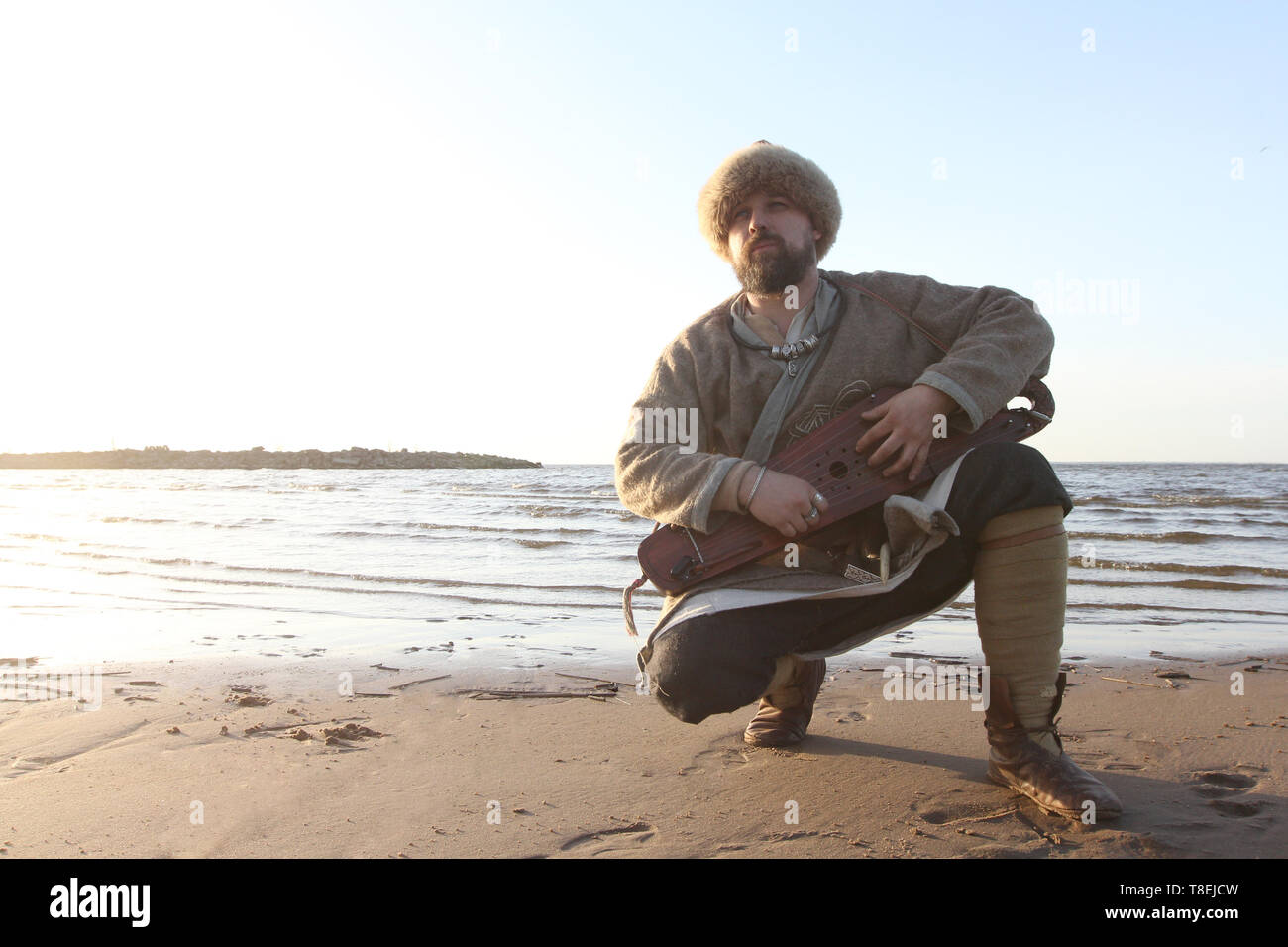 Man reencator in national costume playing gusli ancient traditional ...