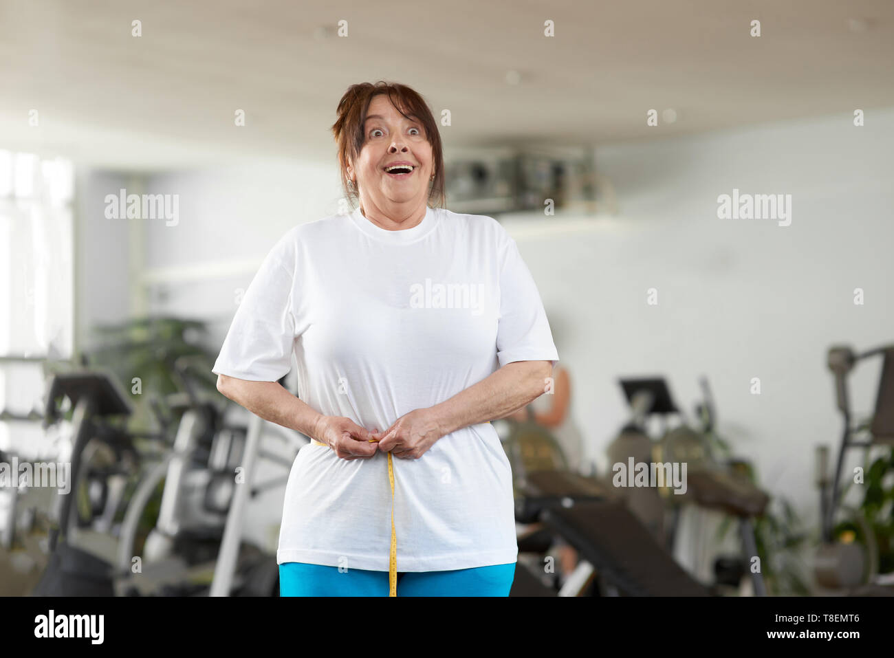 Excited woman measuring her waist at gym. Happy joyful mature lady ...