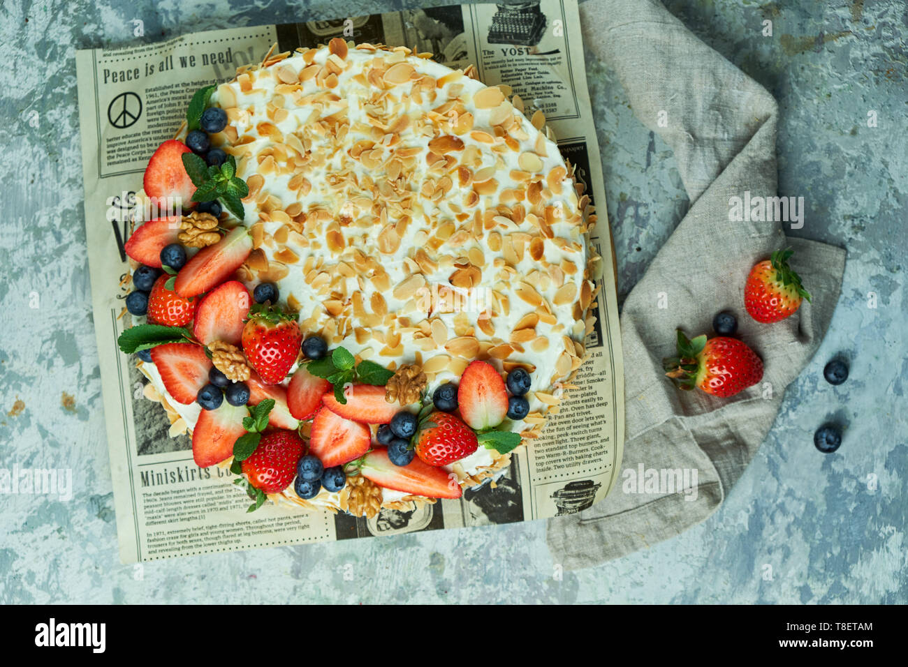 Strawberry meringue cake with almond petals, on newspaper and gray ...