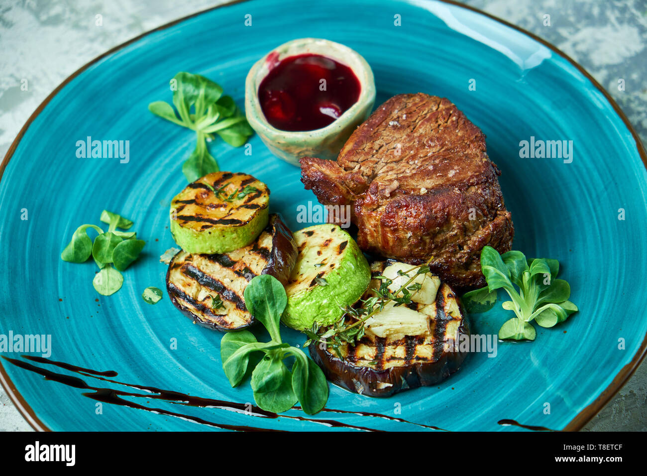 Steak With Barbecue Vegetables And Lingonberry Sauce On A Blue Plate steak-with-barbecue-vegetables-and-lingonberry-sauce-on-a-blue-plate