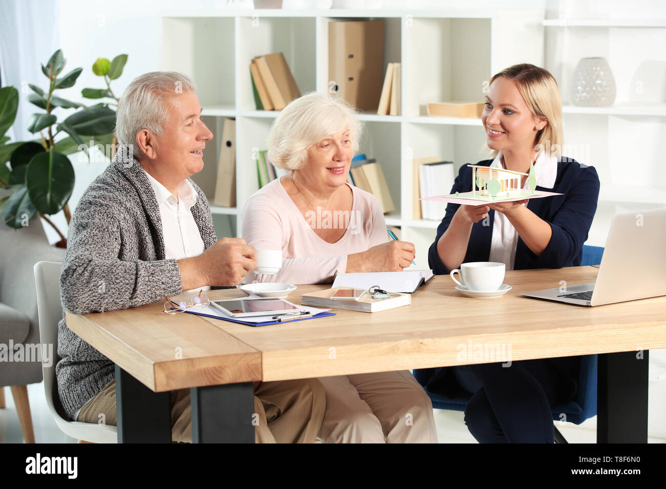 Real estate agent showing model of house to clients in her office Stock ...