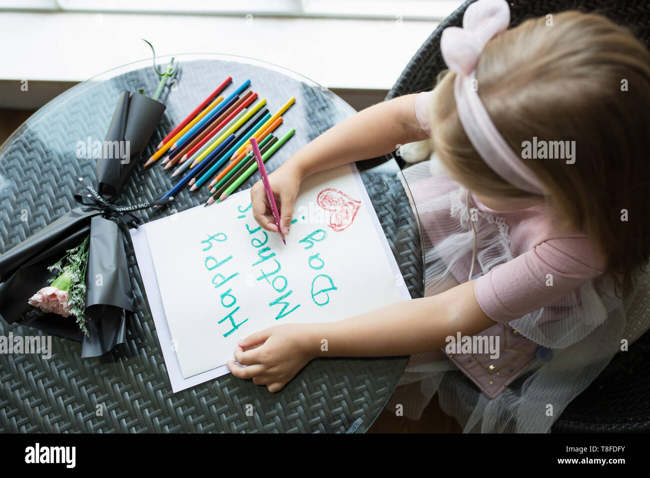 Child daughter painting postcard for mom. Girl sitting at home on table ...
