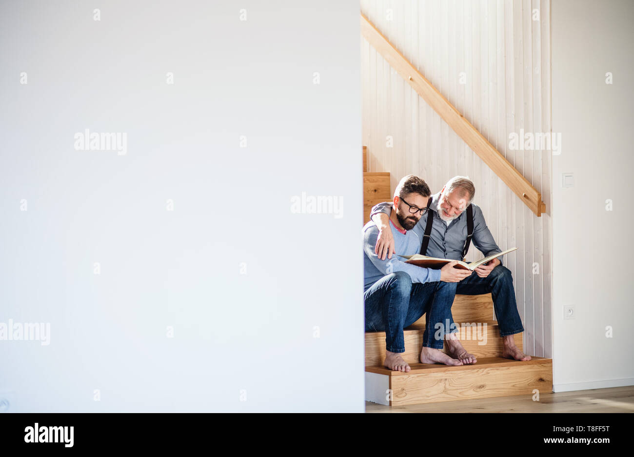 An Adult Son And Senior Father Sitting On Stairs Indoors At Home