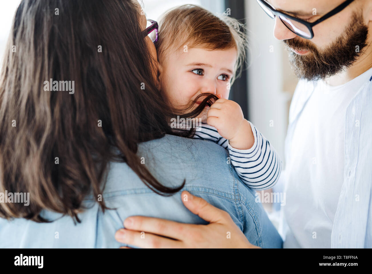 A young family with a crying toddler girl standing indoors at home ...