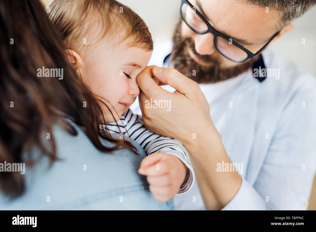 A young family with a crying toddler girl standing indoors at home ...