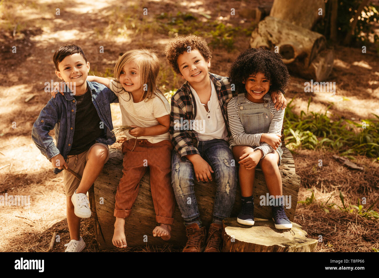 Group of four kids sitting on a wooden log outdoors. Multi-ethnic group ...