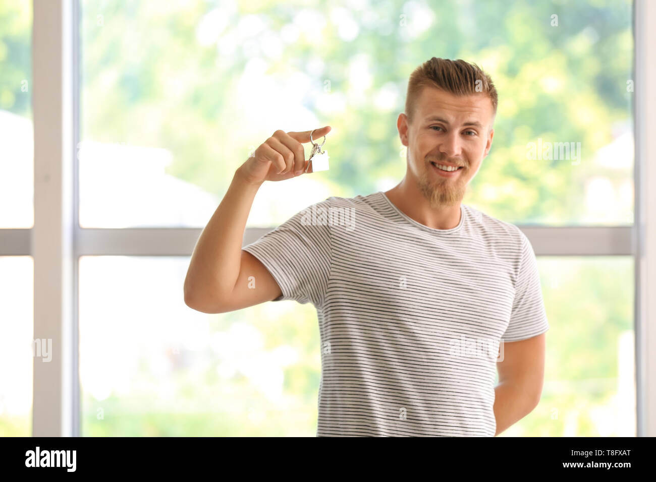 Happy young man with key from his new house indoors Stock Photo - Alamy