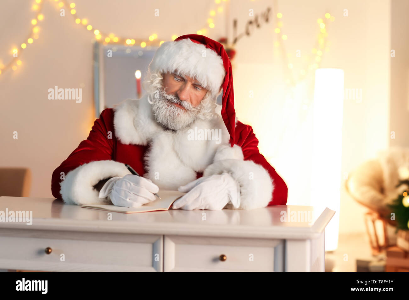 Santa Claus writing in notebook while sitting at table in room ...