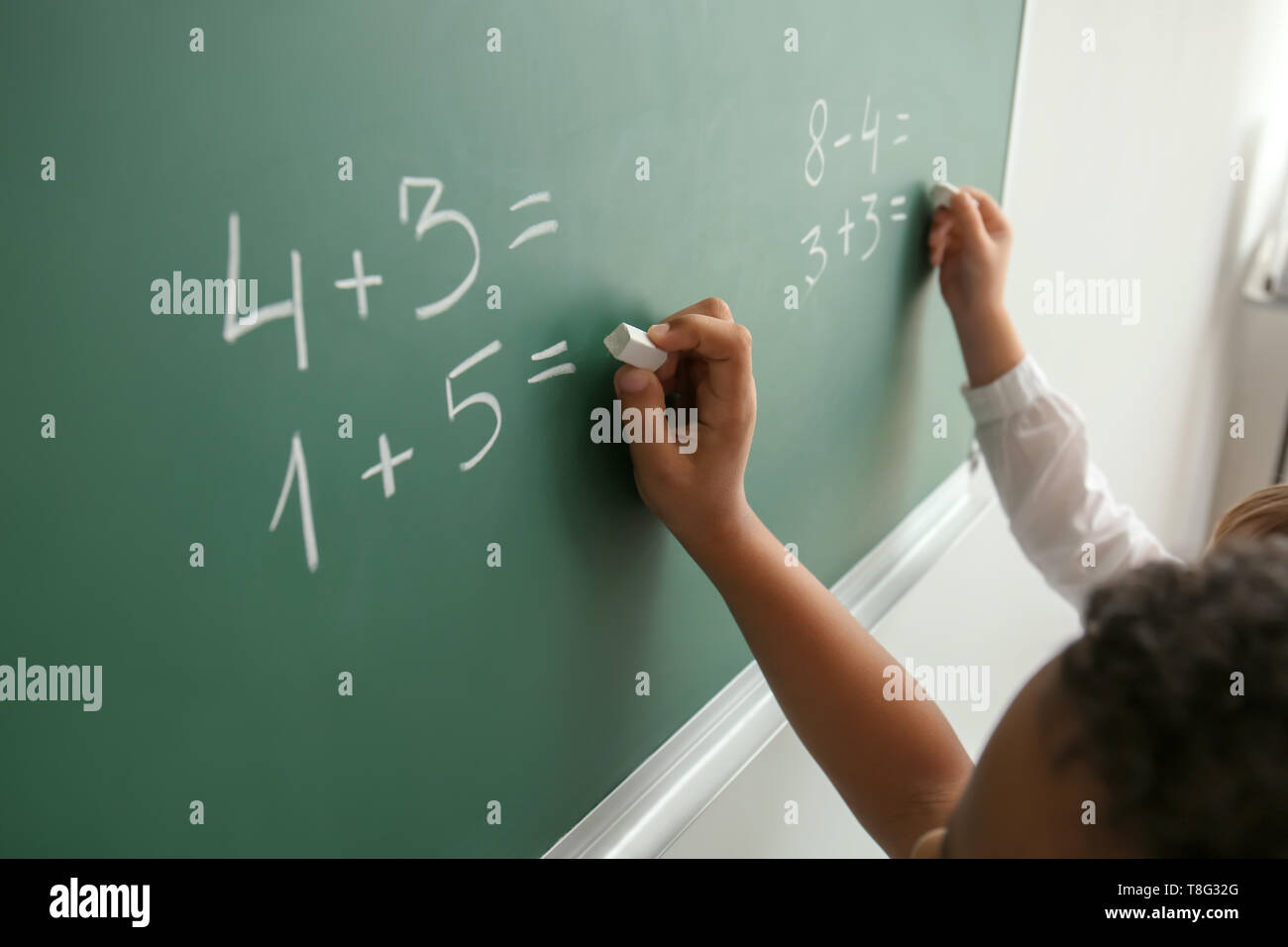 Schoolchildren writing on chalkboard in classroom during math lesson ...