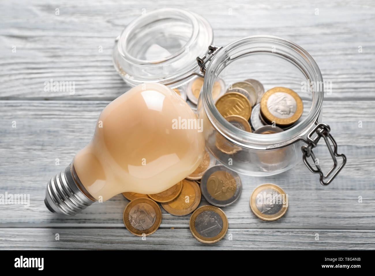 Jar with coins and light bulb on wooden background. Electricity saving ...