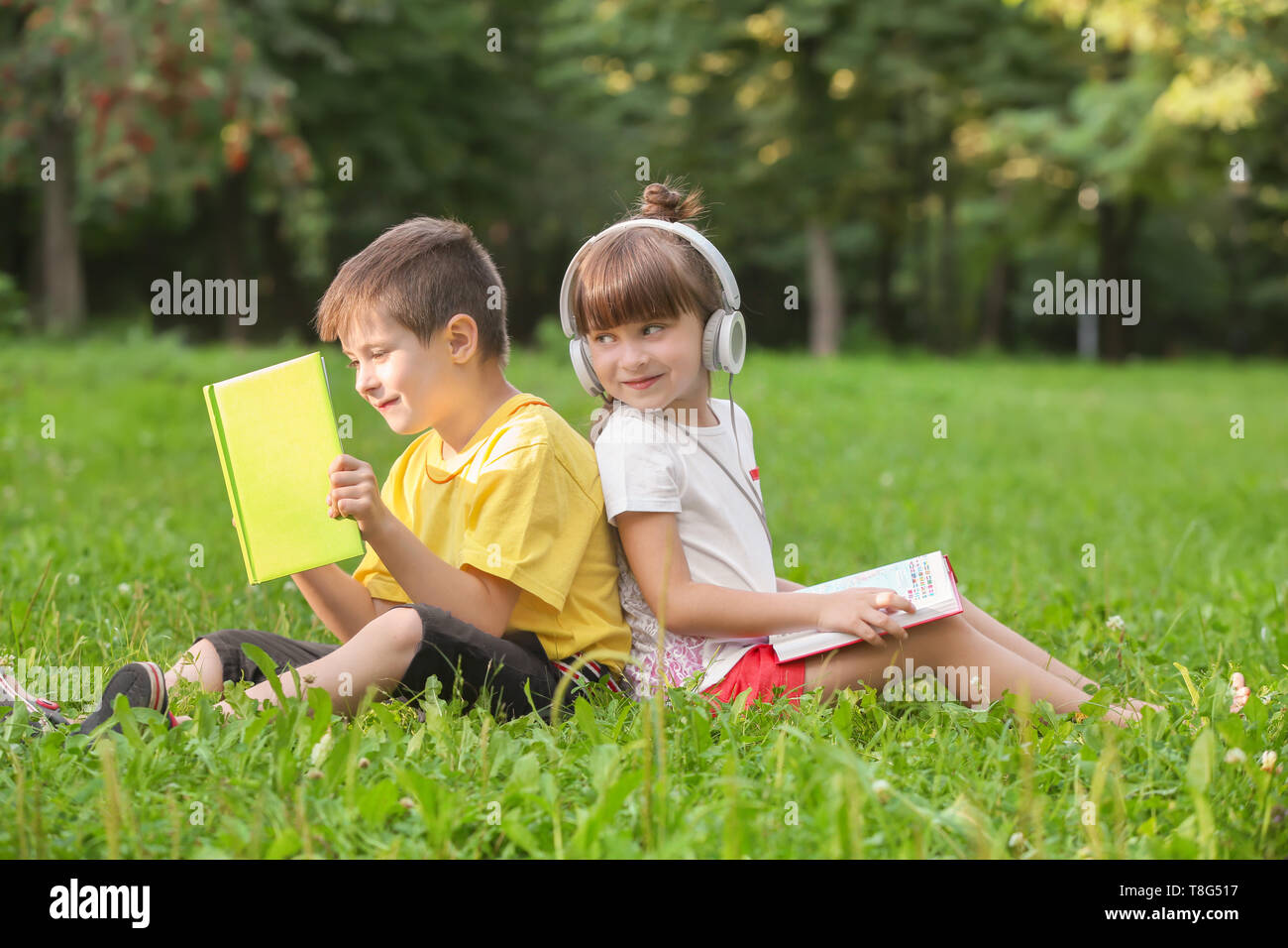 Cute little children reading books and listening to music in park on ...