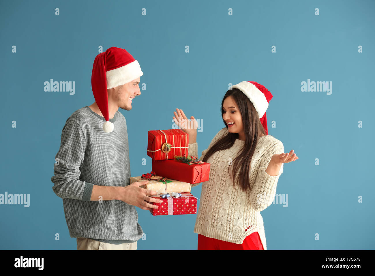 Happy young woman receiving Christmas gifts from her husband on color ...