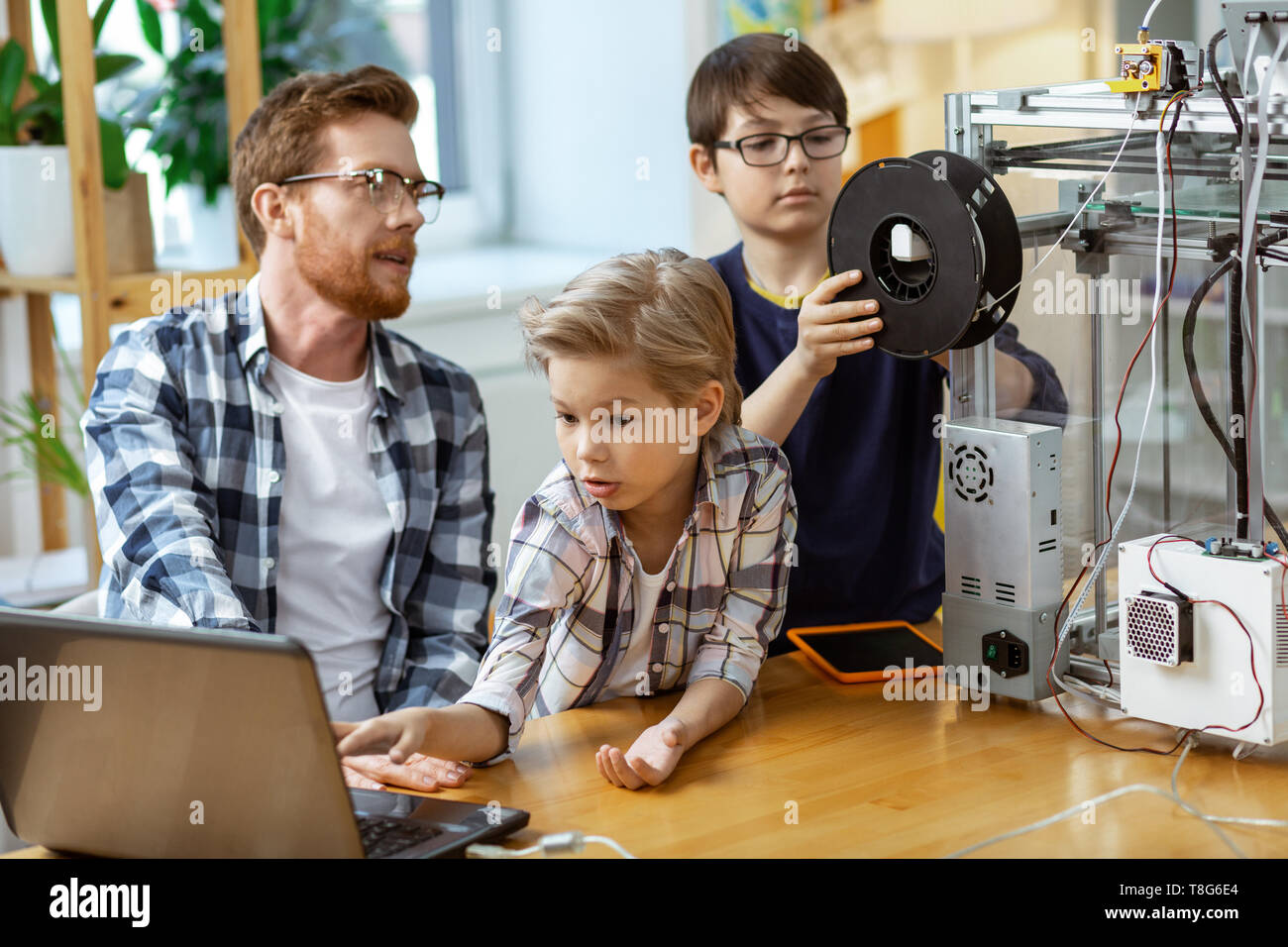 Expressive blonde kid observing laptop screen while his dark-haired ...