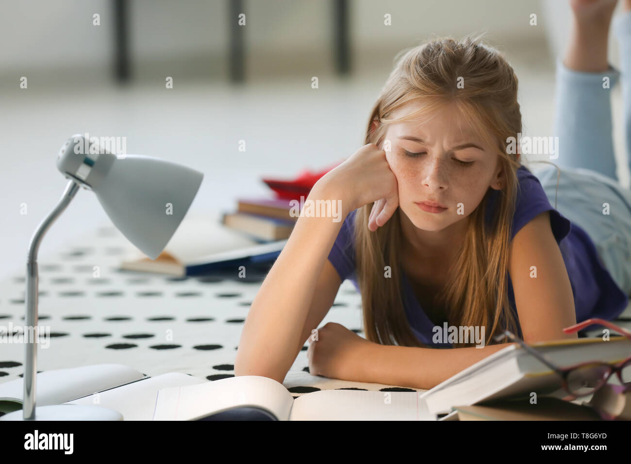 Bored schoolgirl doing homework while lying on floor indoors Stock ...