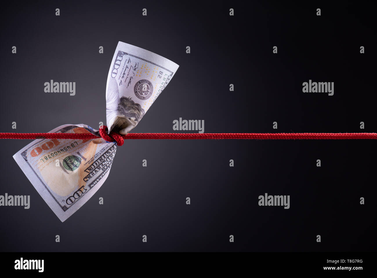 American dollar tied up in red rope knot on dark background with copy ...