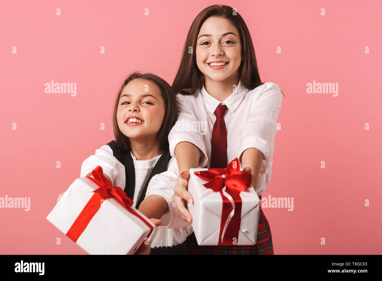 Portrait of little girls in school uniform holding present boxes while ...