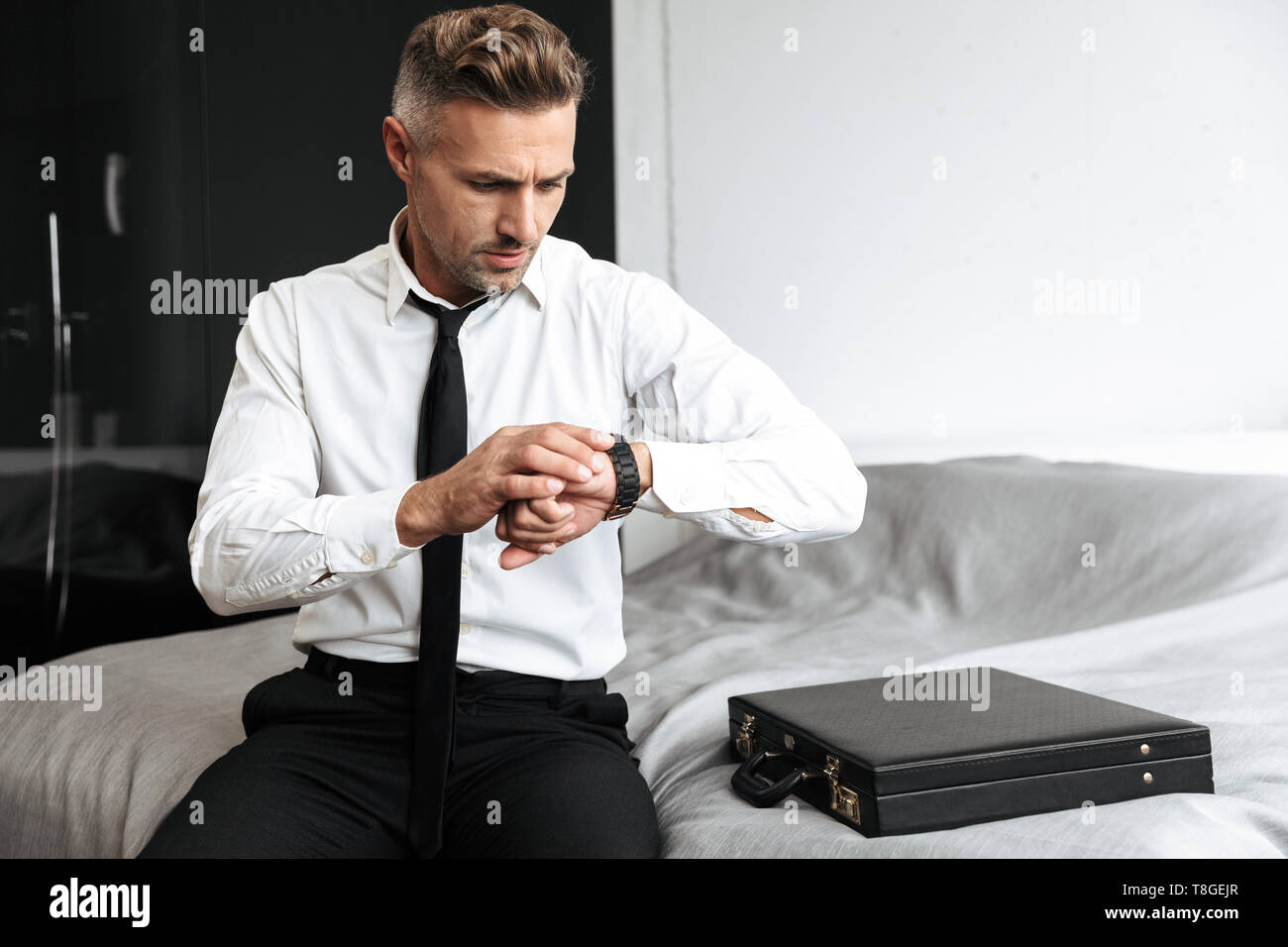 Image of a confused business man in bedroom indoors at home sitting on ...