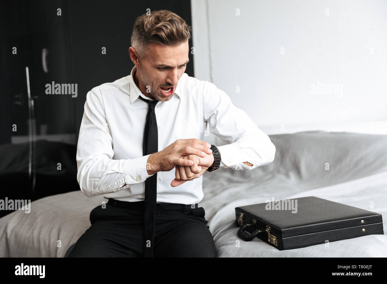 Image of a confused business man in bedroom indoors at home sitting on ...