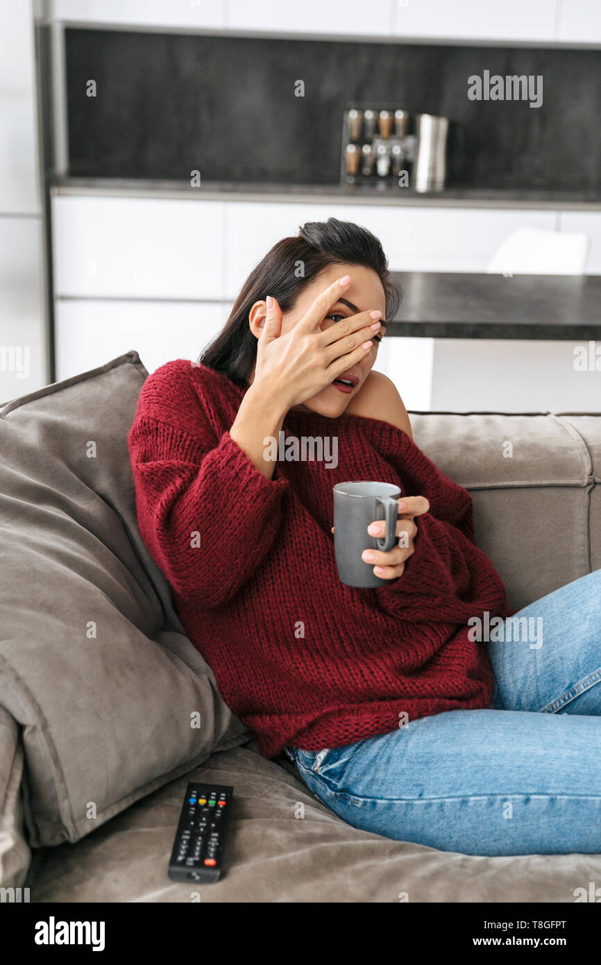 Image of a scared emotional woman indoors in home on sofa watch TV ...