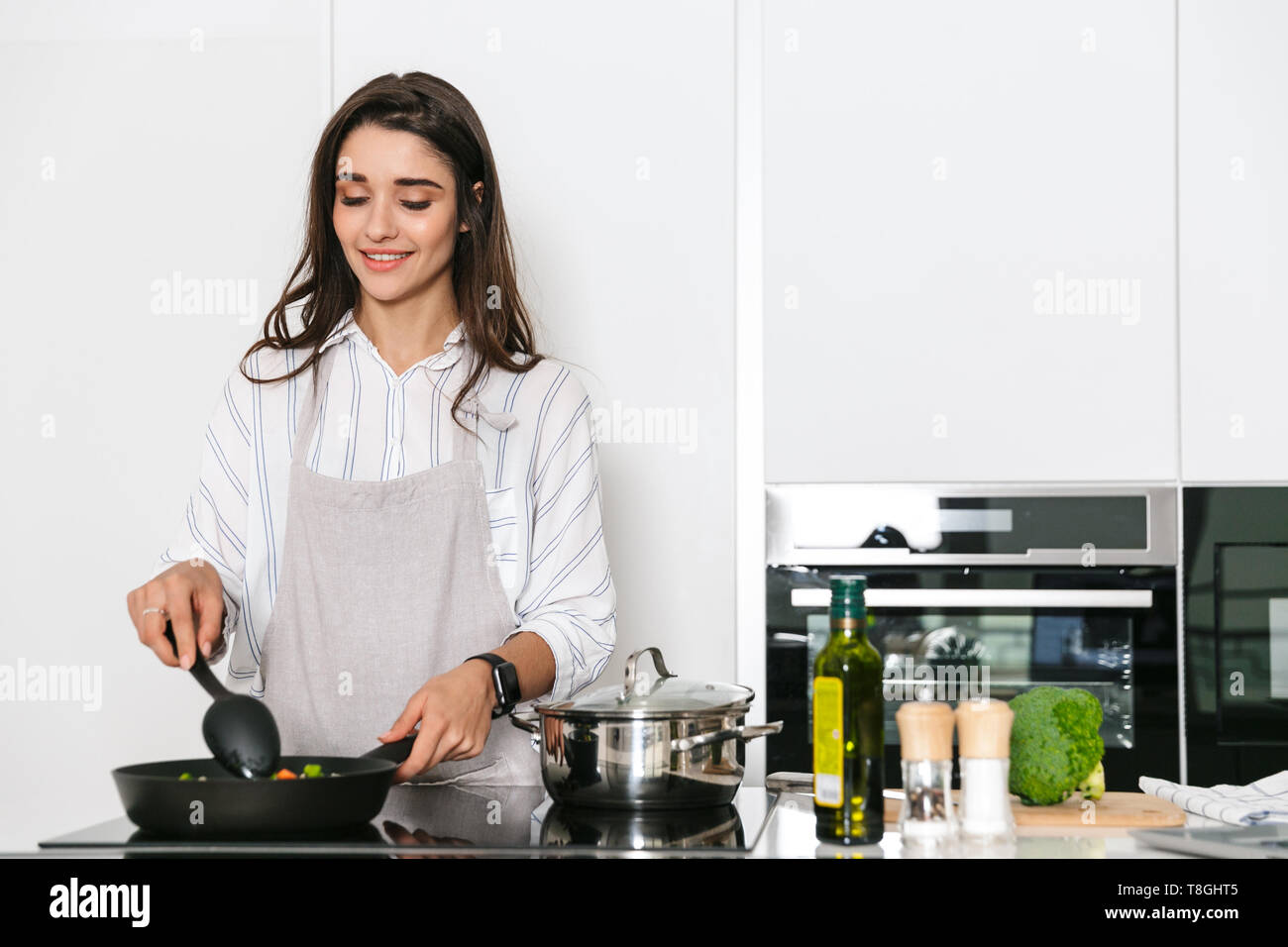 Beautiful young woman cooking healthy dinner at the kitchen, using frying pan Stock Photo - Alamy