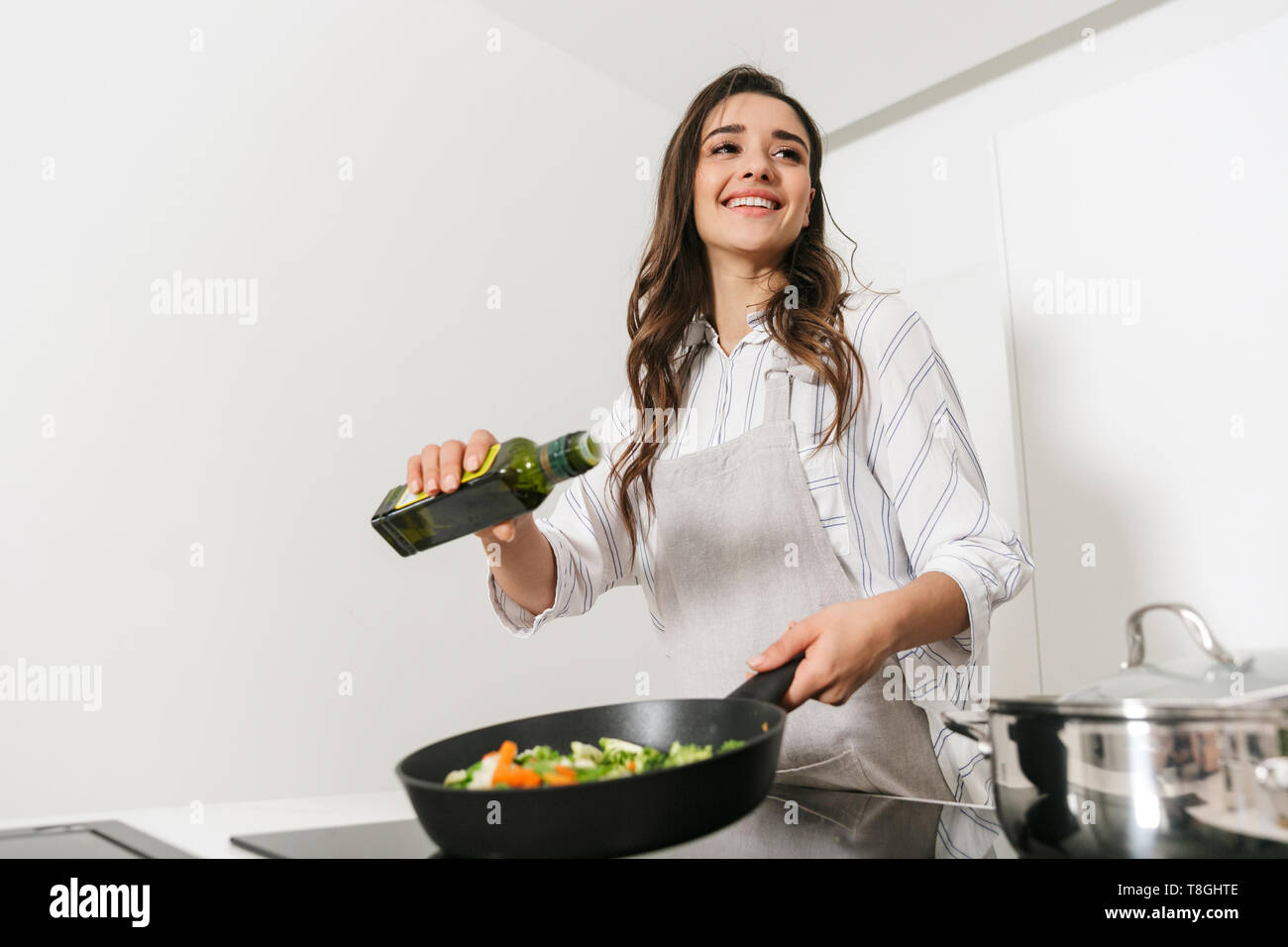 Beautiful young woman cooking healthy dinner at the kitchen, using frying pan Stock Photo - Alamy